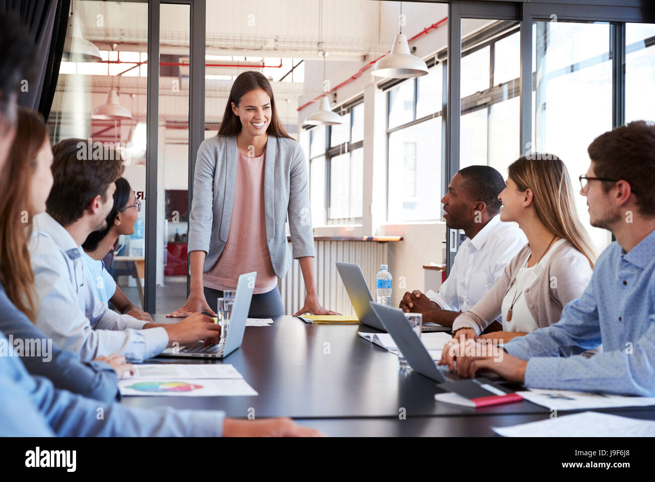 Woman addressing team leans on desk at business meeting Stock Photo - Alamy