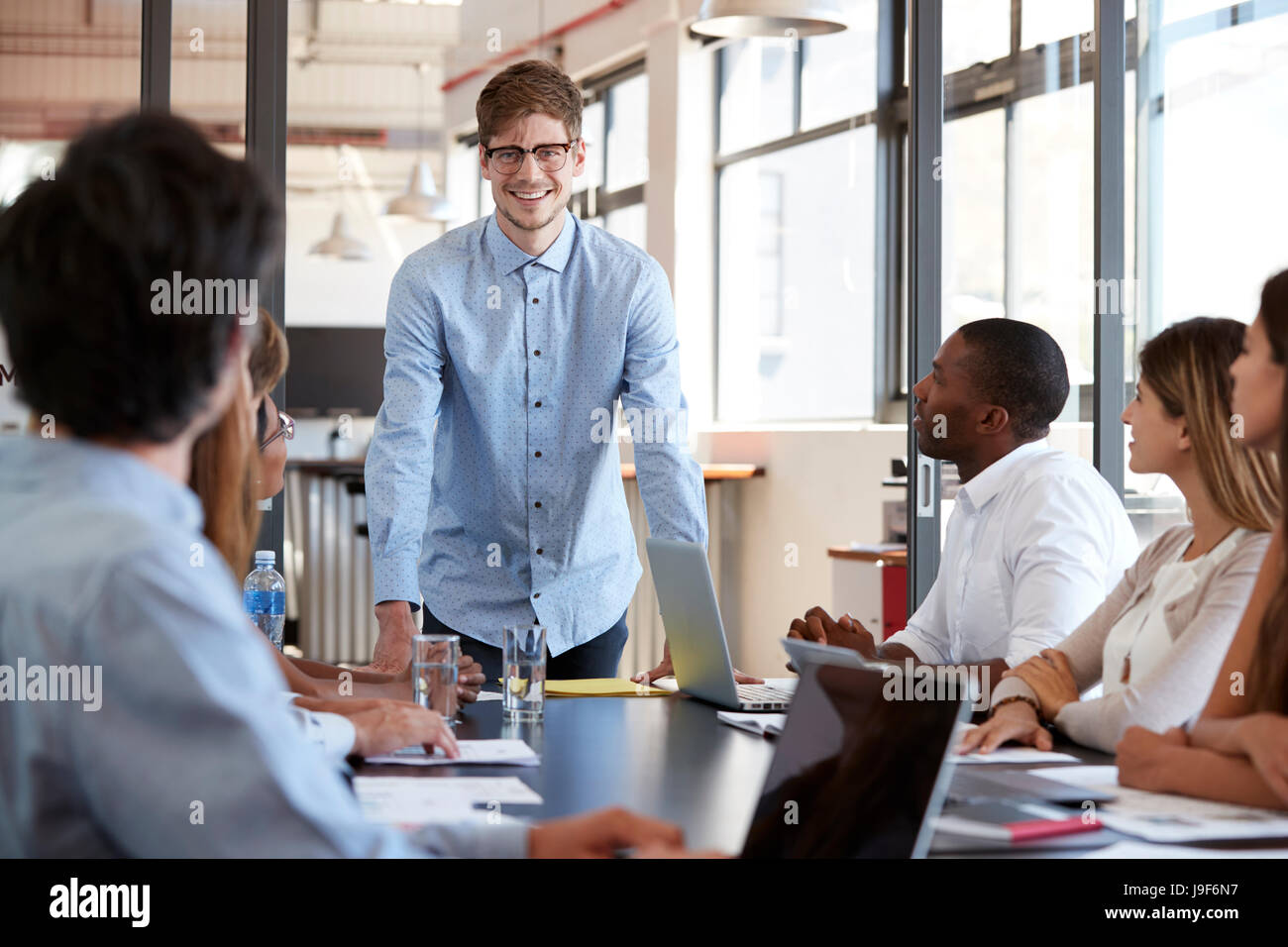 Happy young man stands addressing team at business meeting Stock Photo ...