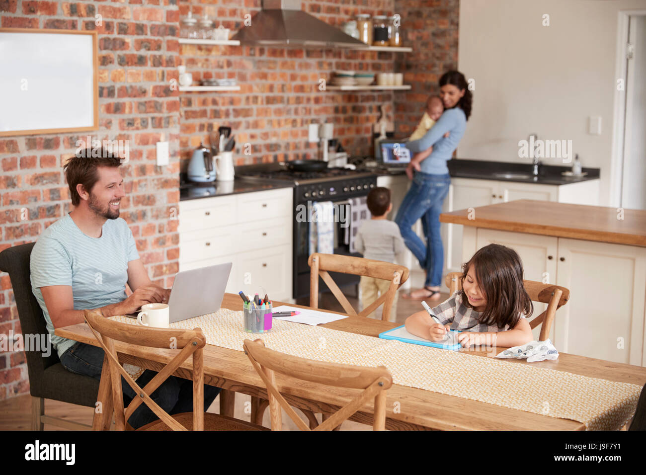 Busy Family Home With Father Working As Mother Prepares Meal Stock ...