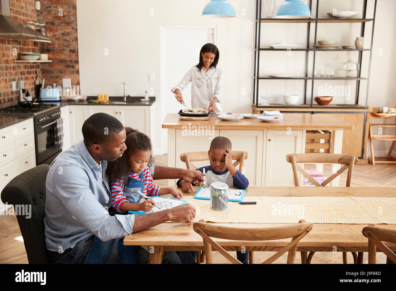 Father And Children Drawing At Table As Mother Prepares Meal Stock ...