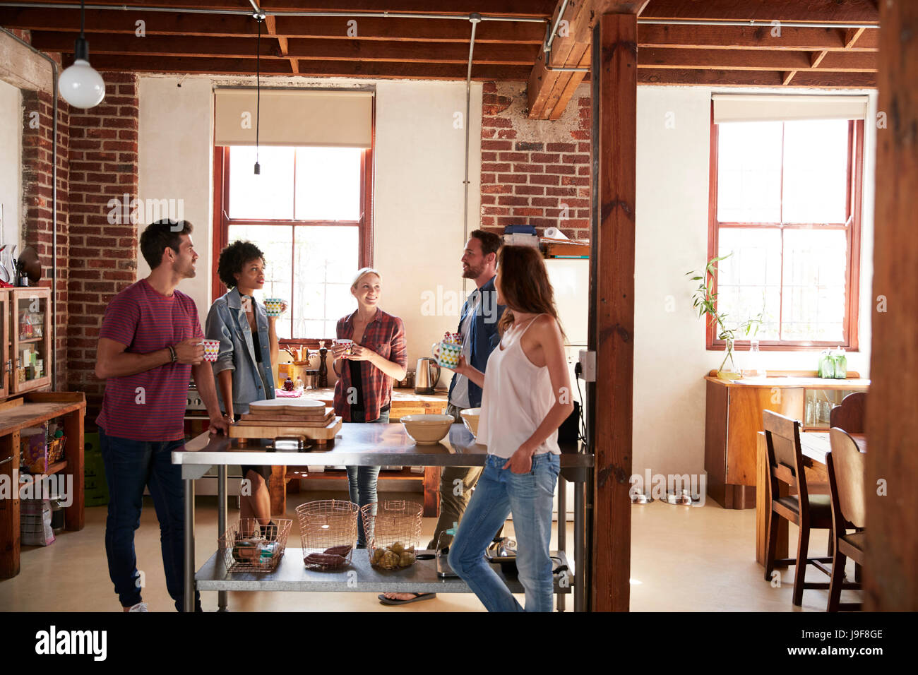 Friends talking over coffee in kitchen, three quarter length Stock ...
