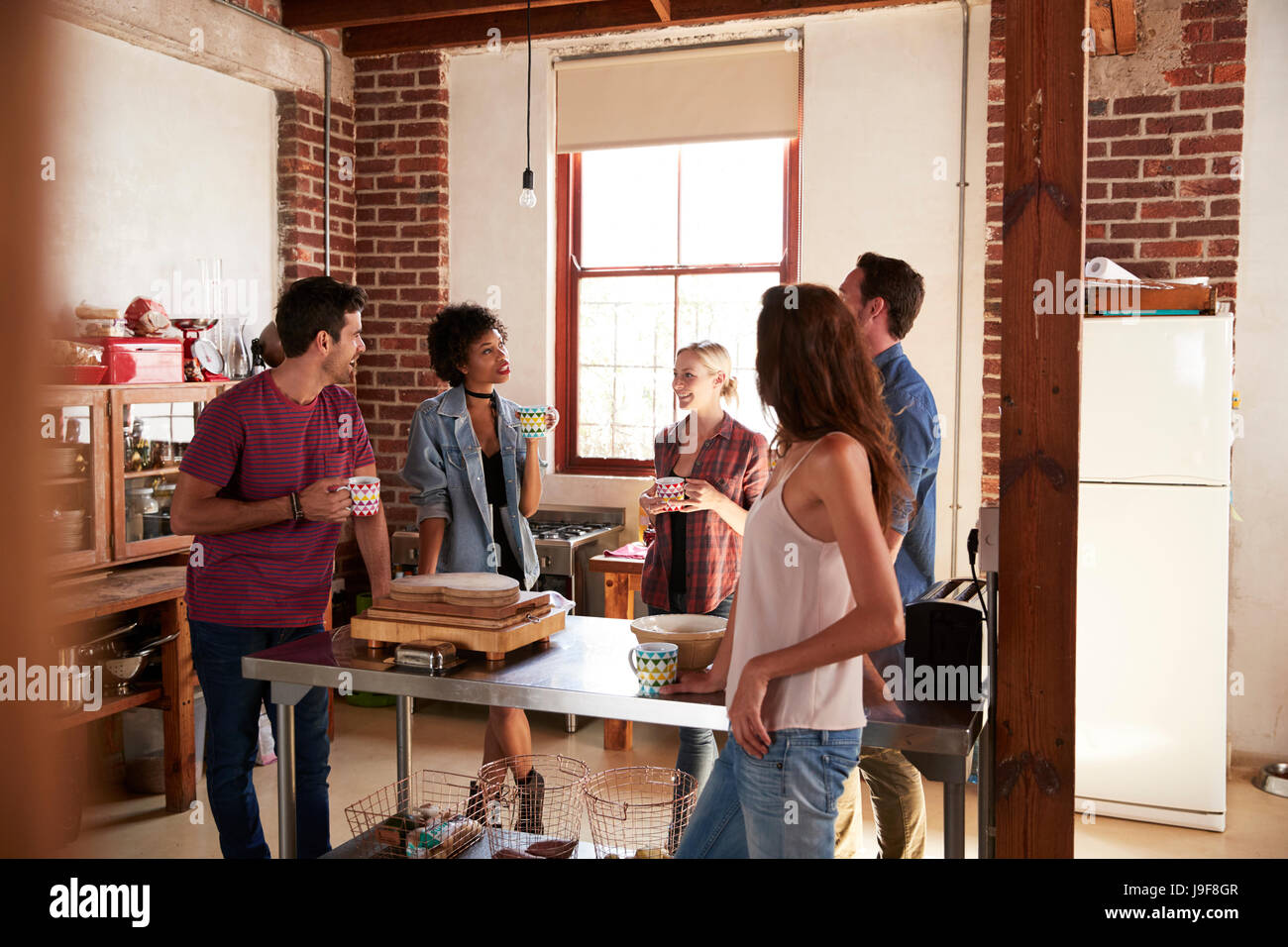 Friends talking over coffee in kitchen, three quarter length Stock ...