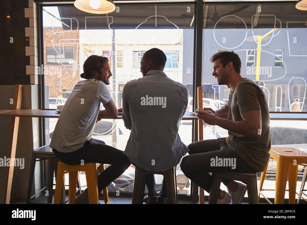 Rear View Of Three Male Friends Meeting In Coffee Shop Stock Photo - Alamy