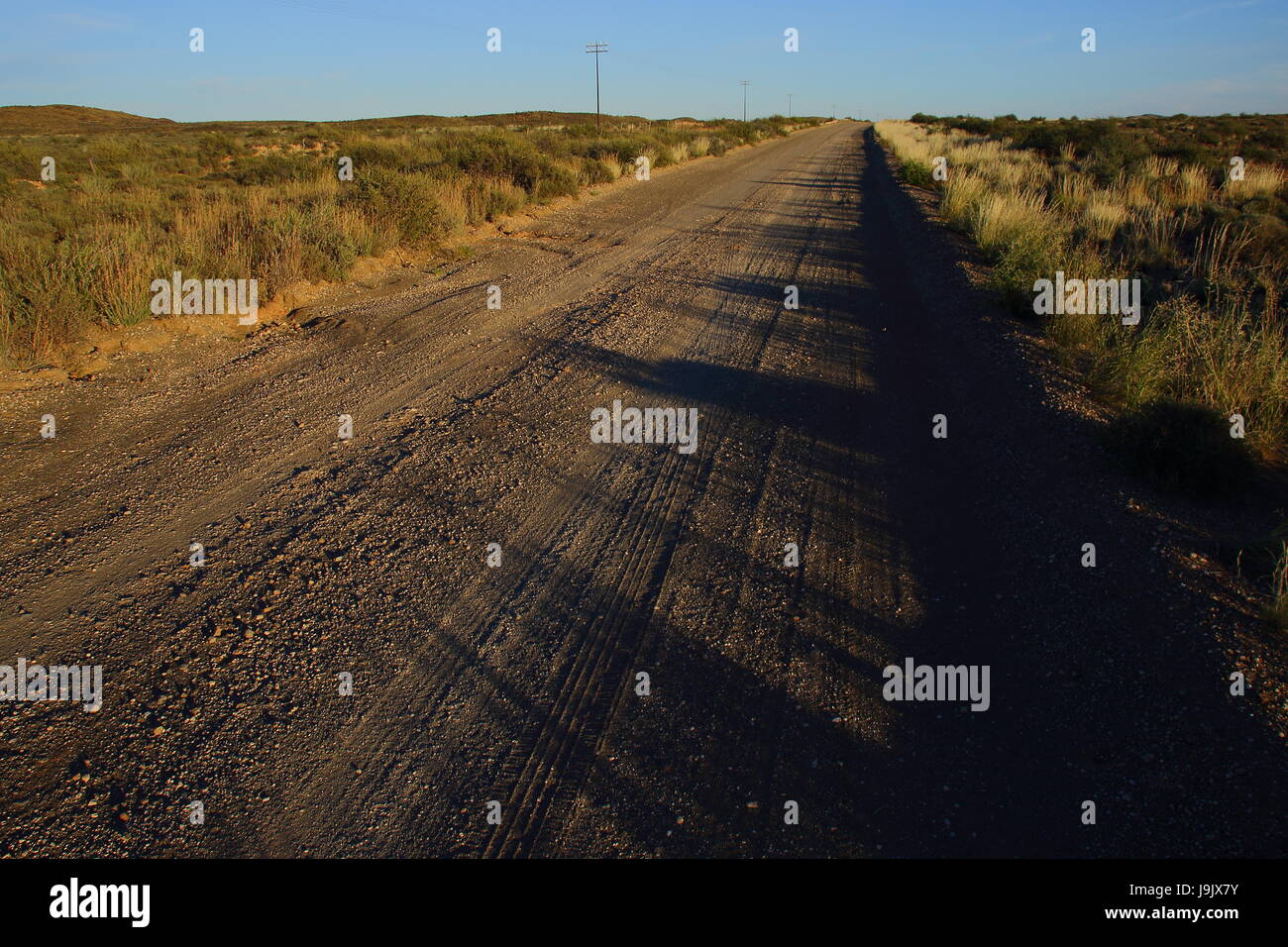 A dusty dirt road with early morning shadows lead to a clear blue ...