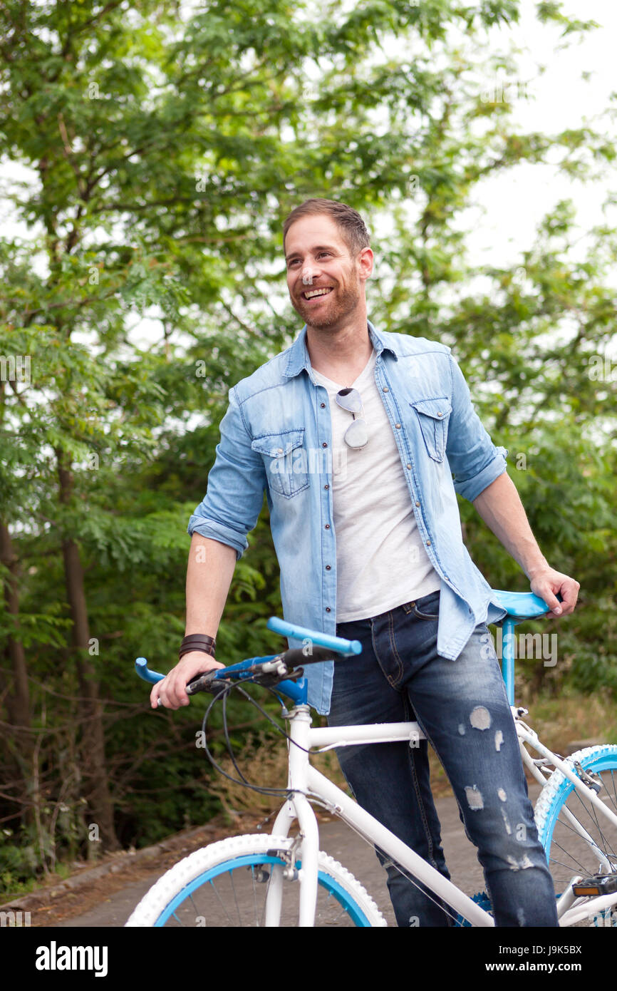 Handsome man with denim clothes enjoying with his bike in the park ...