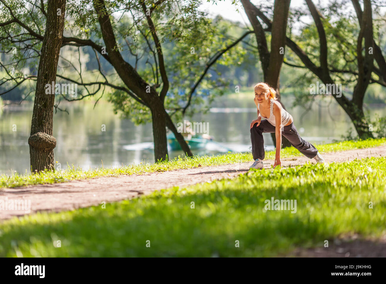 Young woman jogging stretching in summer park near river Stock Photo ...