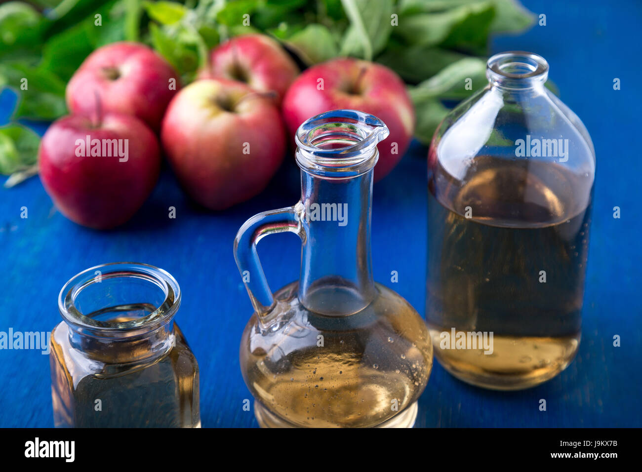 Apple cider vinegar. Three glass bottle on blue background. Red apples ...