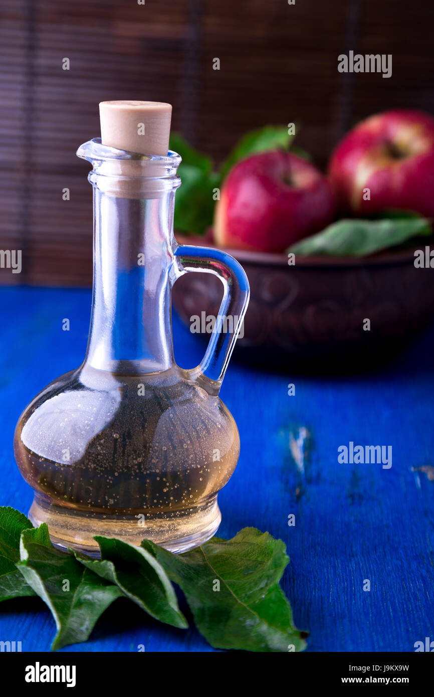 Apple cider vinegar in glass bottle on blue background. Red apples in ...