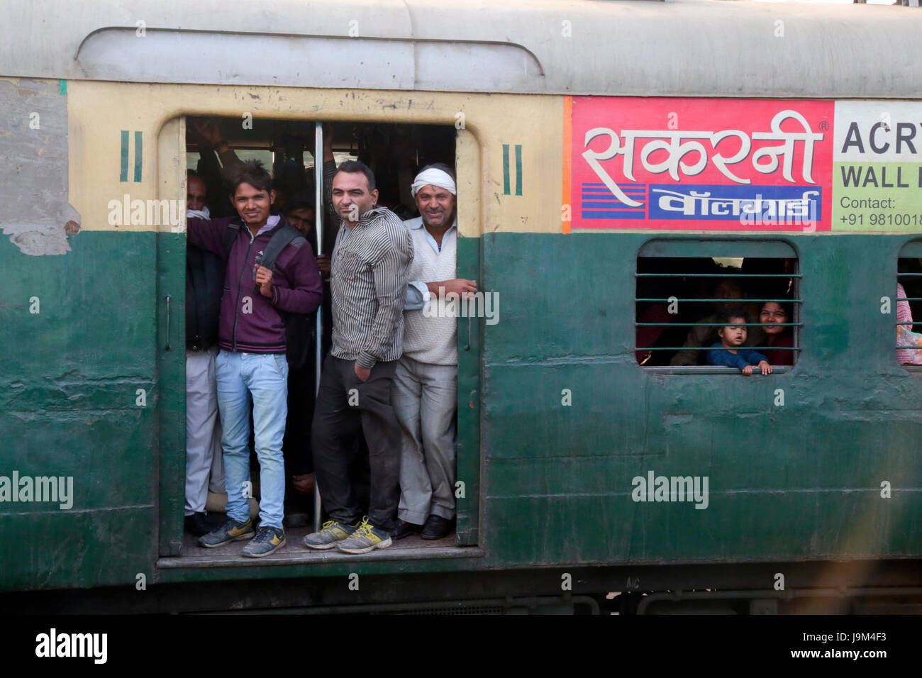 People hanging from open doors of commuter train passing through Delhi ...