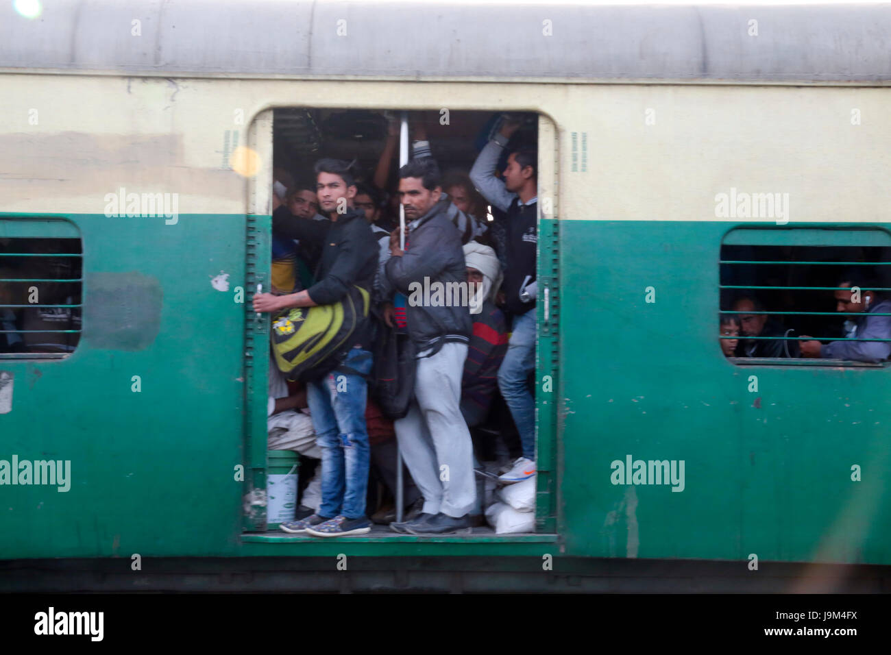 People hanging from open doors of commuter train passing through Delhi ...