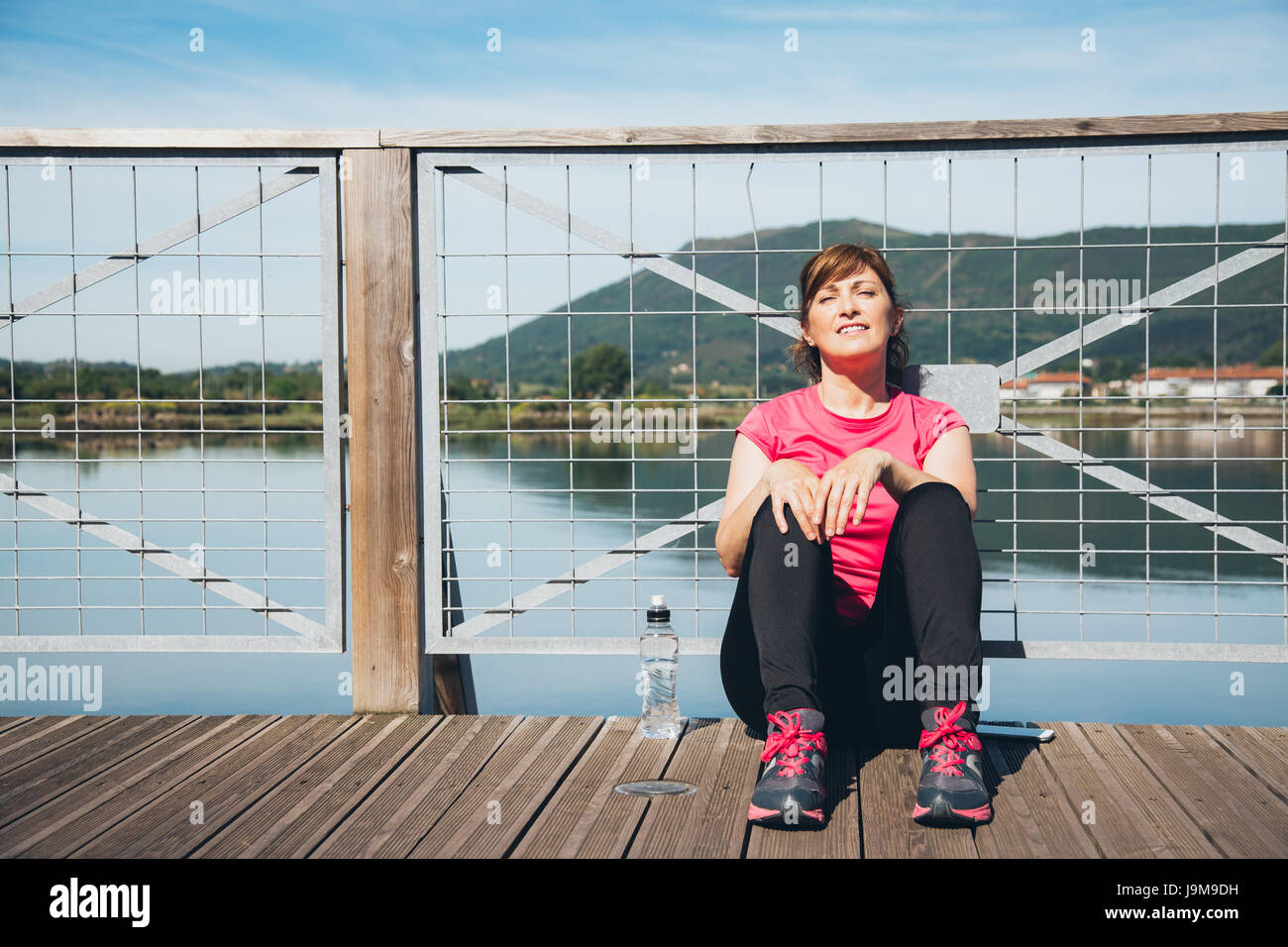 Middle aged woman relaxing after running enjoying the sun leaning on a ...