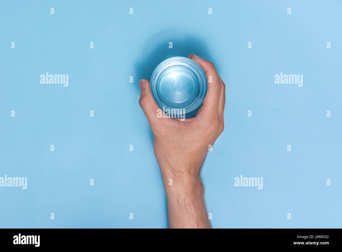 Hand holding water glass on blue background Stock Photo - Alamy
