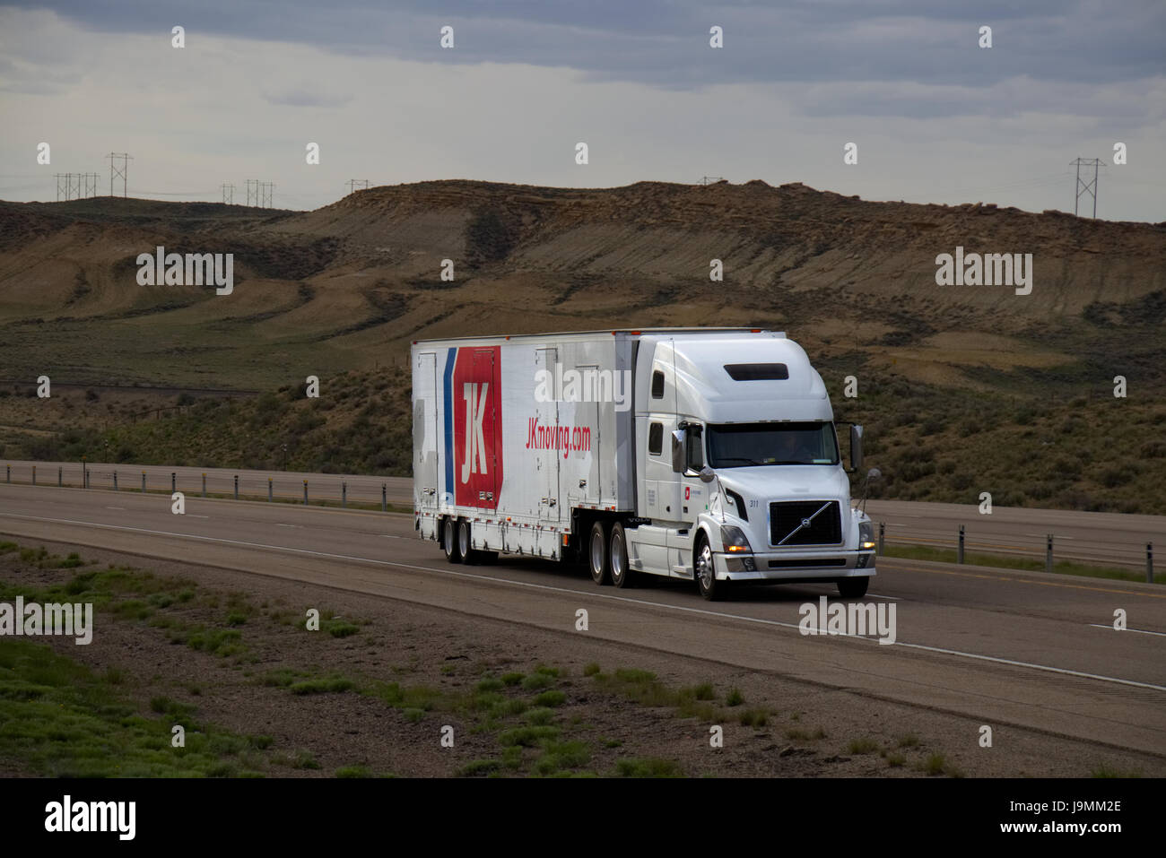 A White Volvo-Semi-Truck Pulls a White "JK Moving" Trailer along a ...