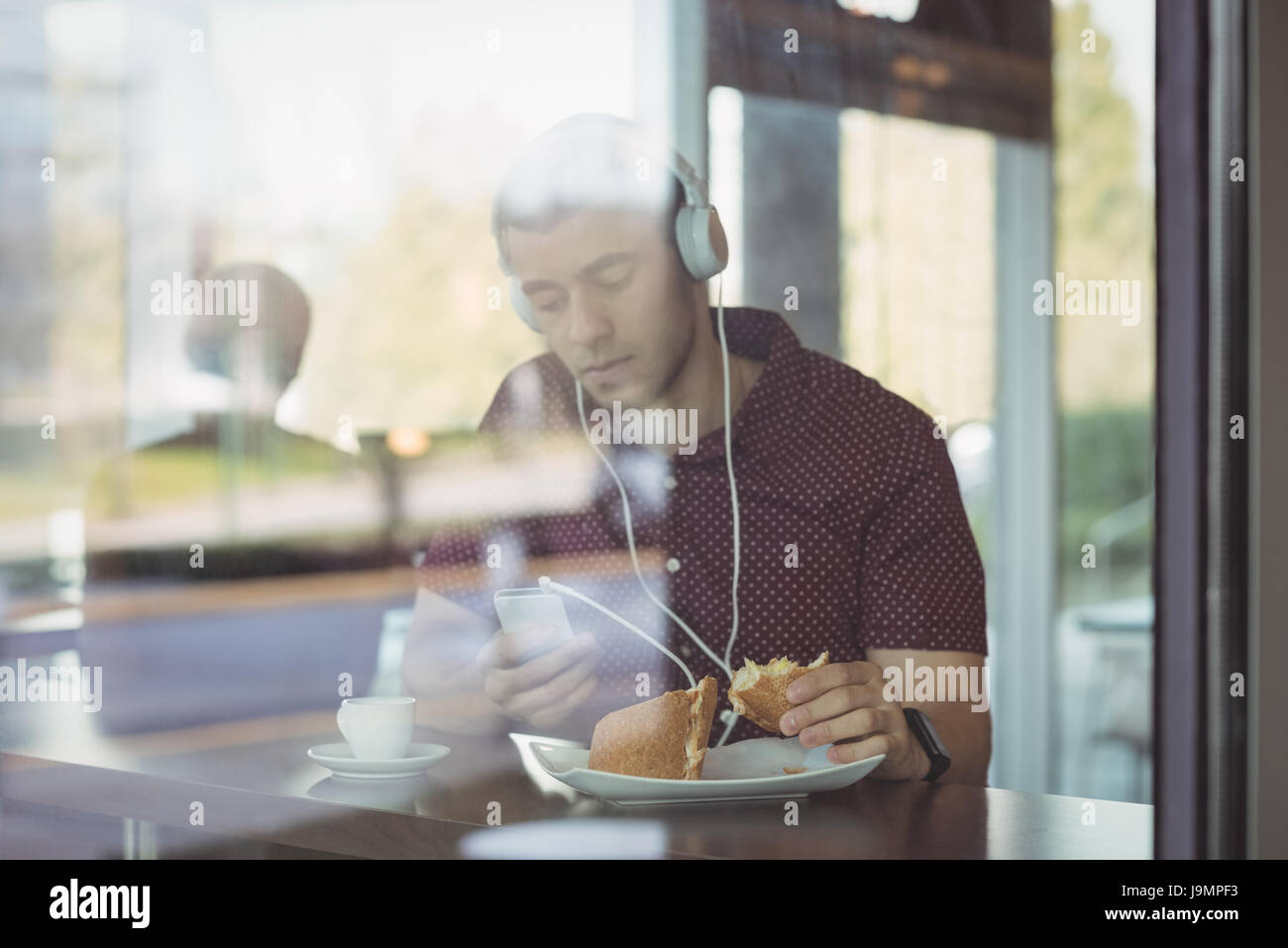 Male executive with headphones using mobile phone in office cafeteria ...