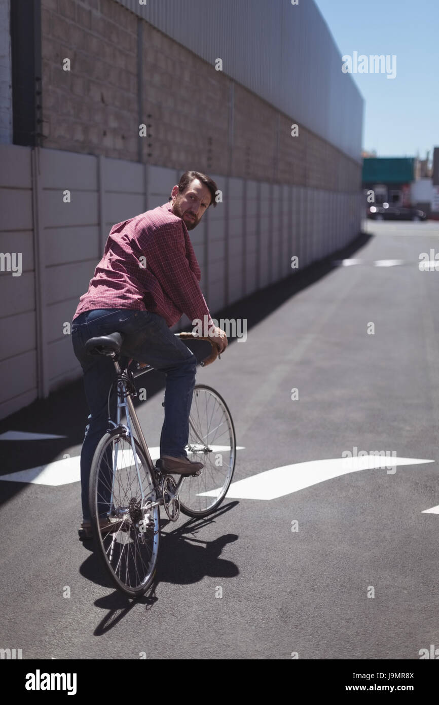 Full length of man looking over shoulder while riding bicycle on road ...