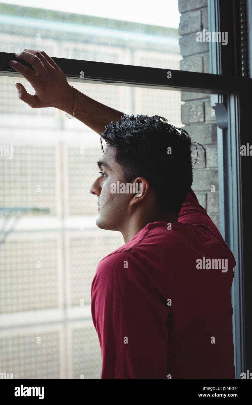 Thoughtful man looking through window at home Stock Photo - Alamy