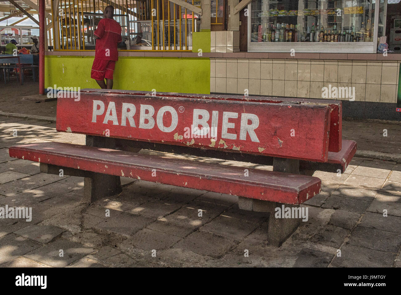 Red bench in Paramaribo, Suriname with Parbo beer advertisement. A ...