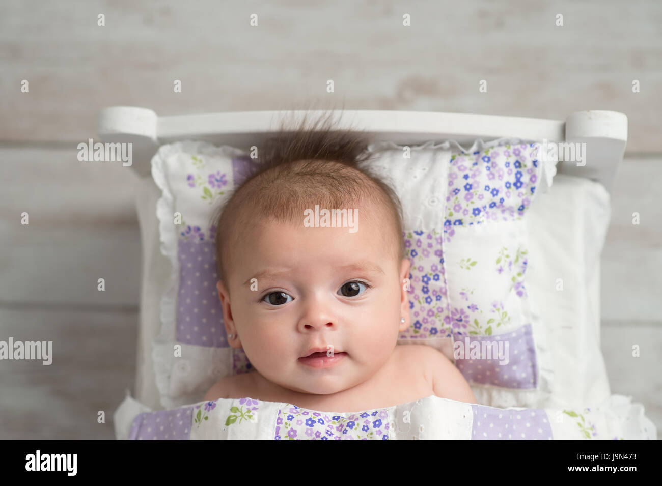 An overhead shot of a four month old, alert, baby girl. She is lying in ...