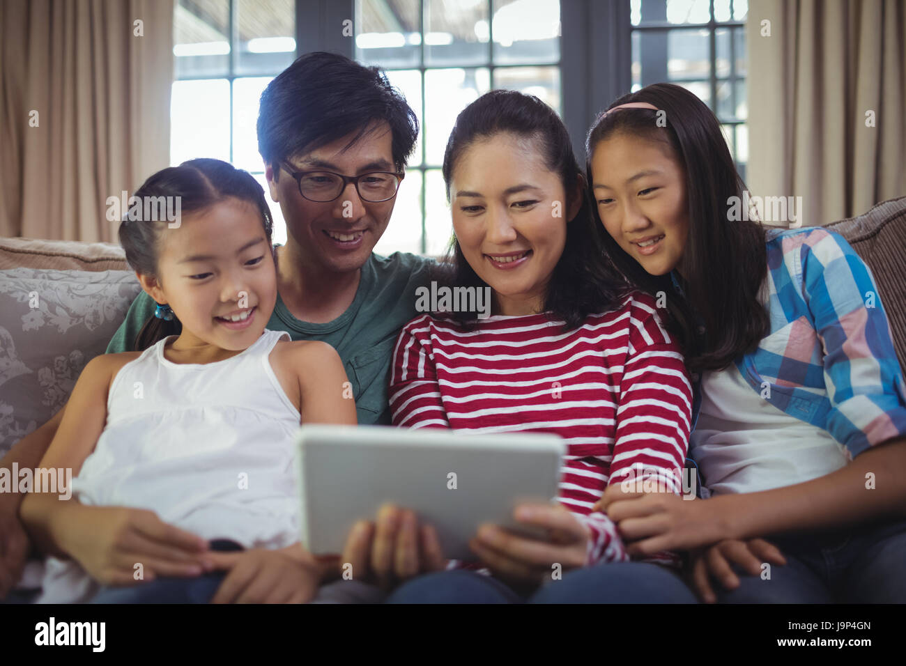 Smiling family using digital tablet together in living room at home ...