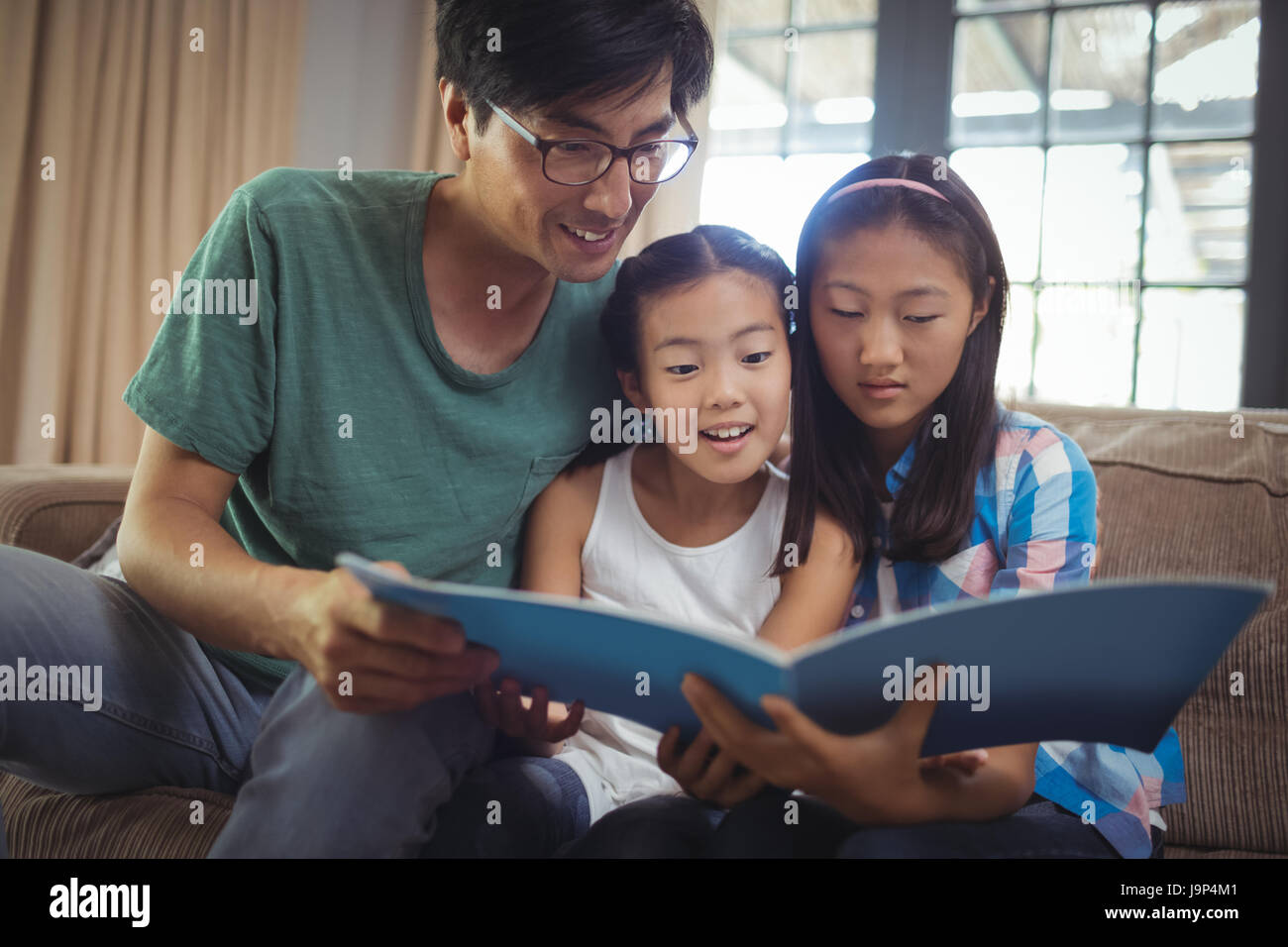 Father and siblings watching photo album together in living room at ...