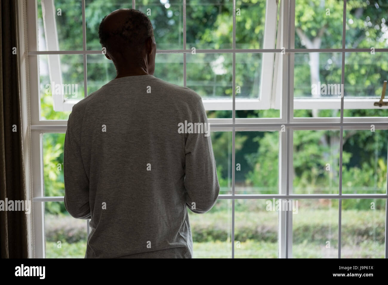 Rear view of senior man standing against windows at home Stock Photo ...