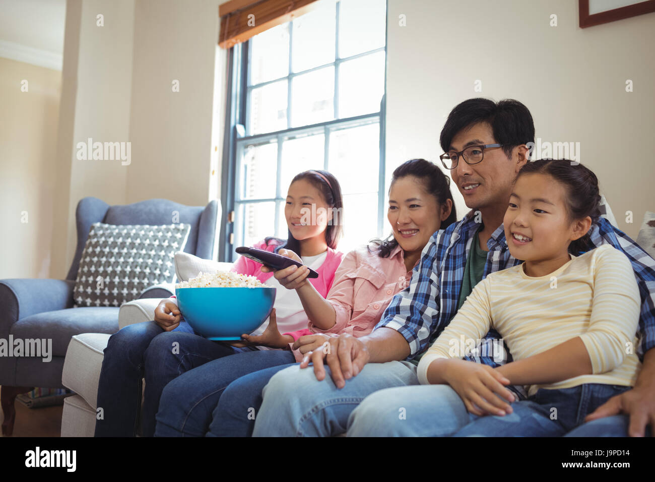 Smiling family watching television together in living room at home ...