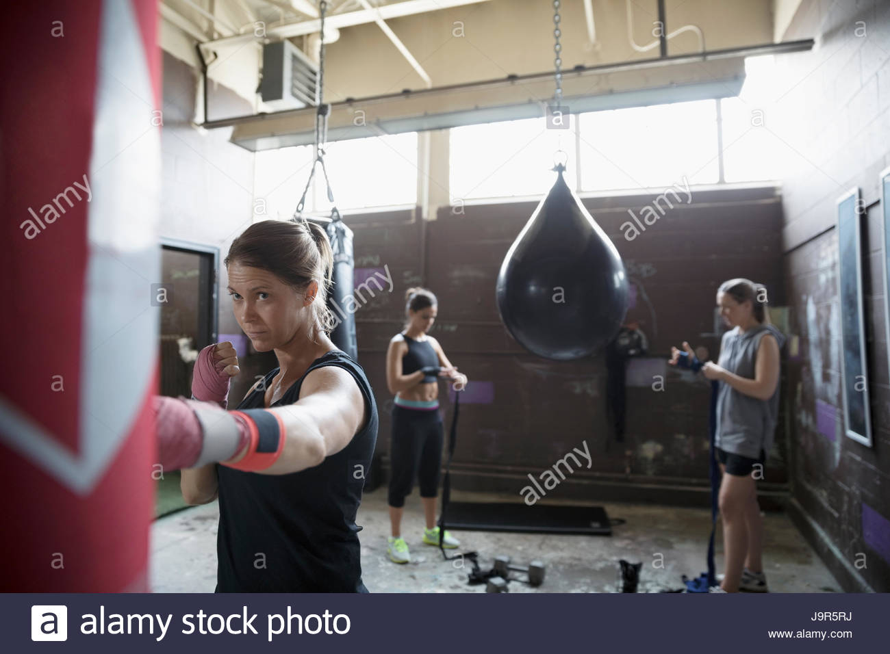 Female boxers wrapping wrists and using punching bags in gritty gym ...