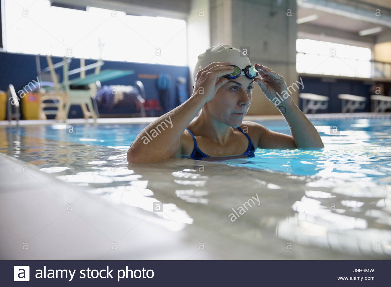 Serious female swimmer adjusting swimming goggles in swimming pool ...