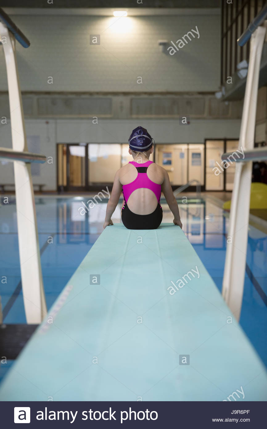 Girl swimmer sitting at the edge of springboard diving board over ...