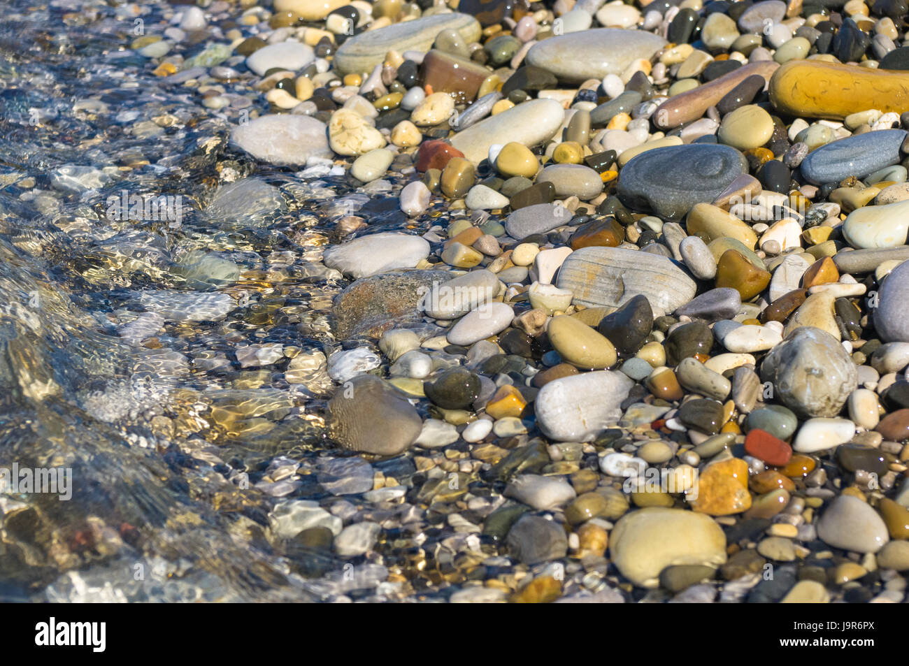 sea pebble beach with multicoloured stones, transparent waves with foam ...