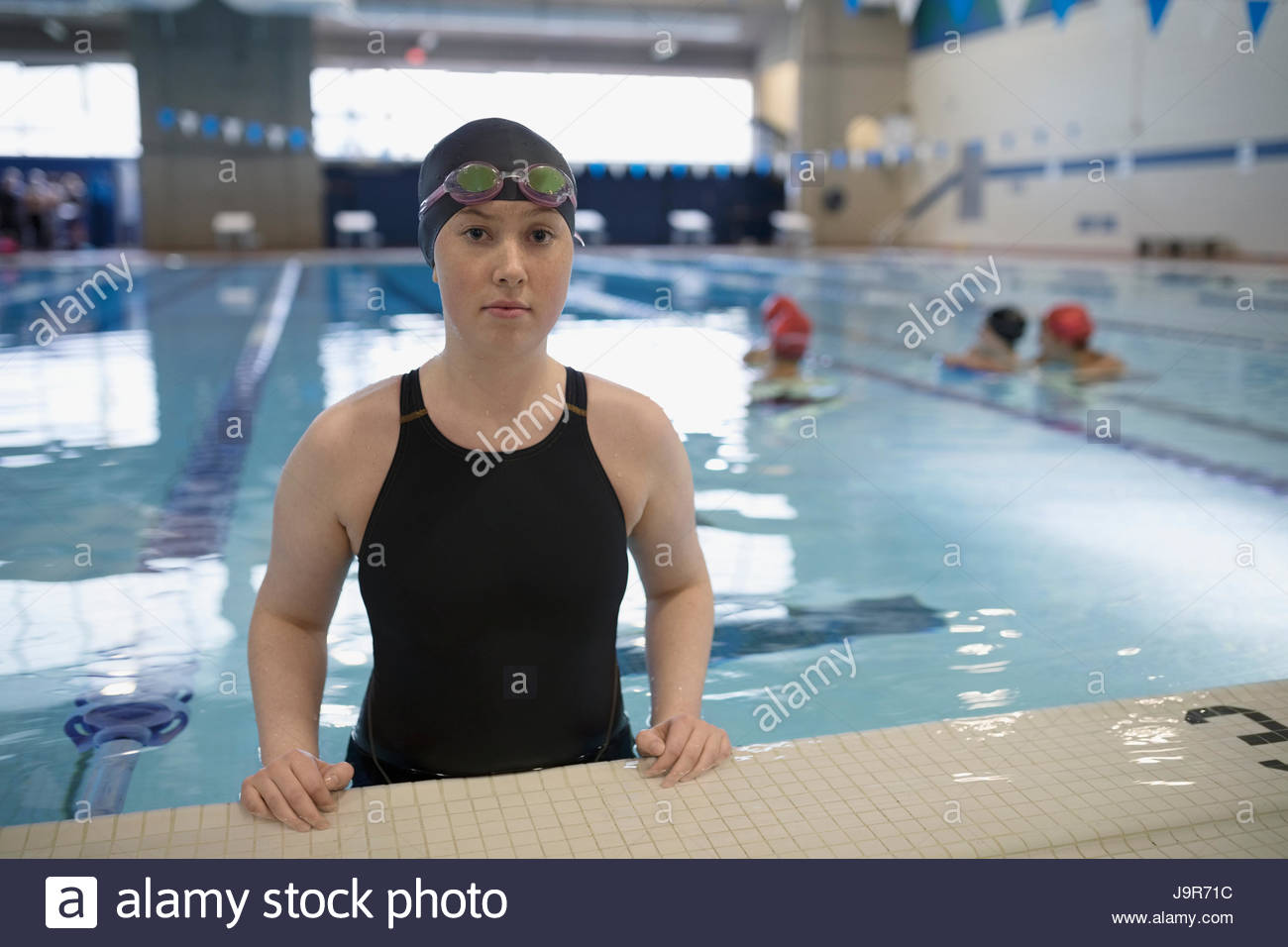 Portrait confident young woman swimmer at edge of swimming pool in ...