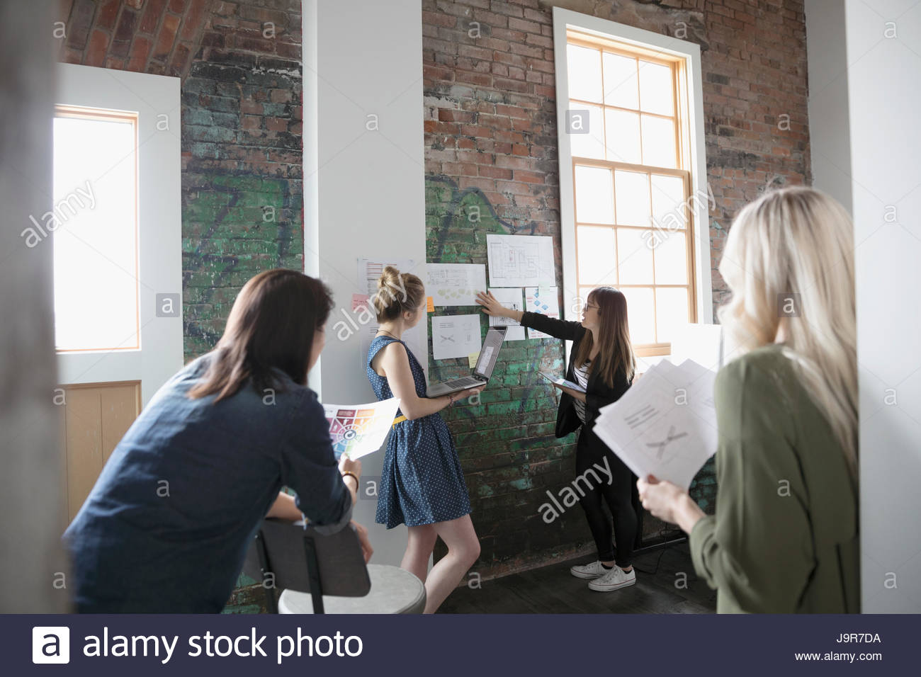 Creative business people meeting, reviewing paperwork hanging on wall ...