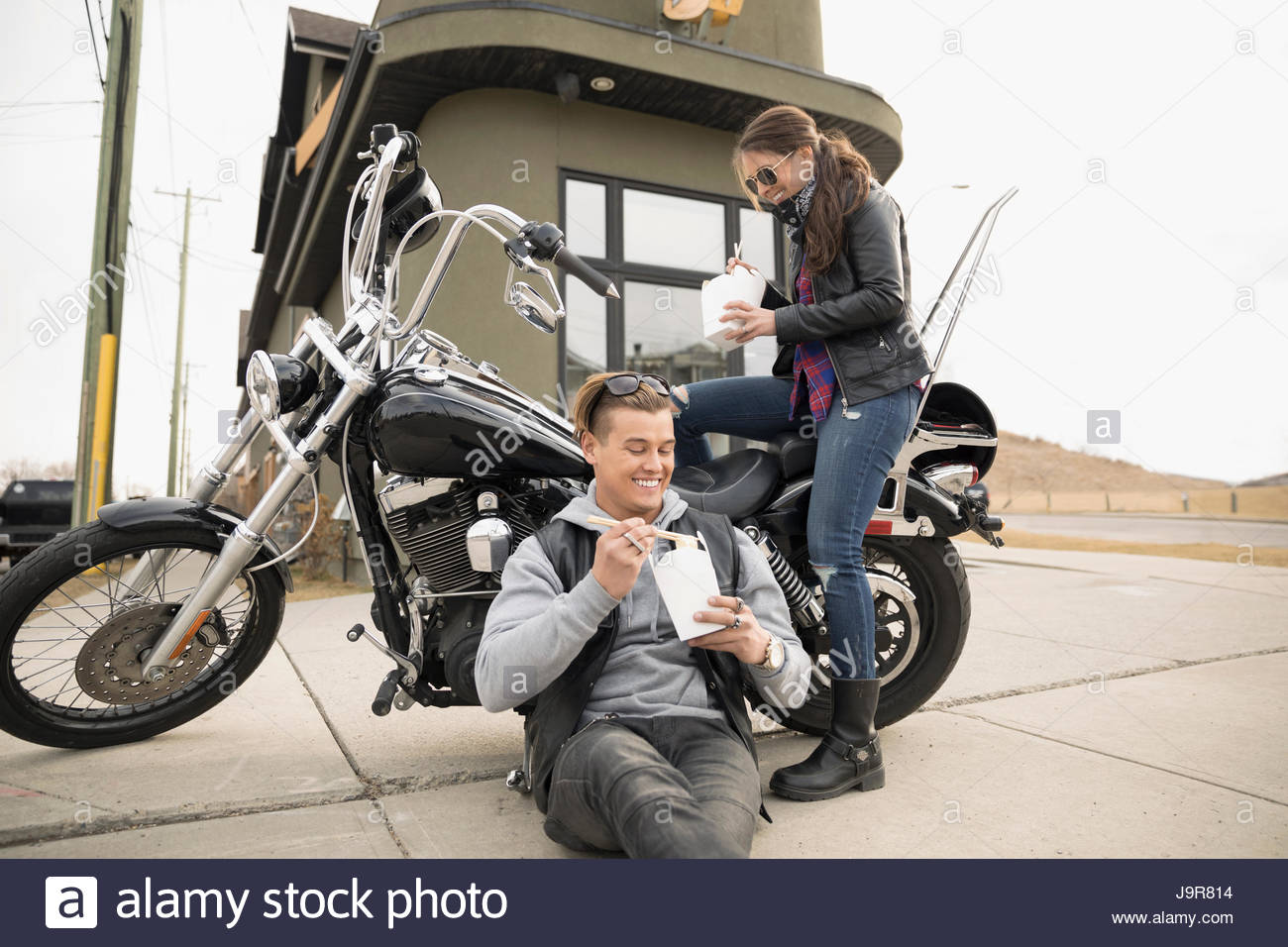 Biker couple eating take out Chinese food at motorcycle in parking lot ...