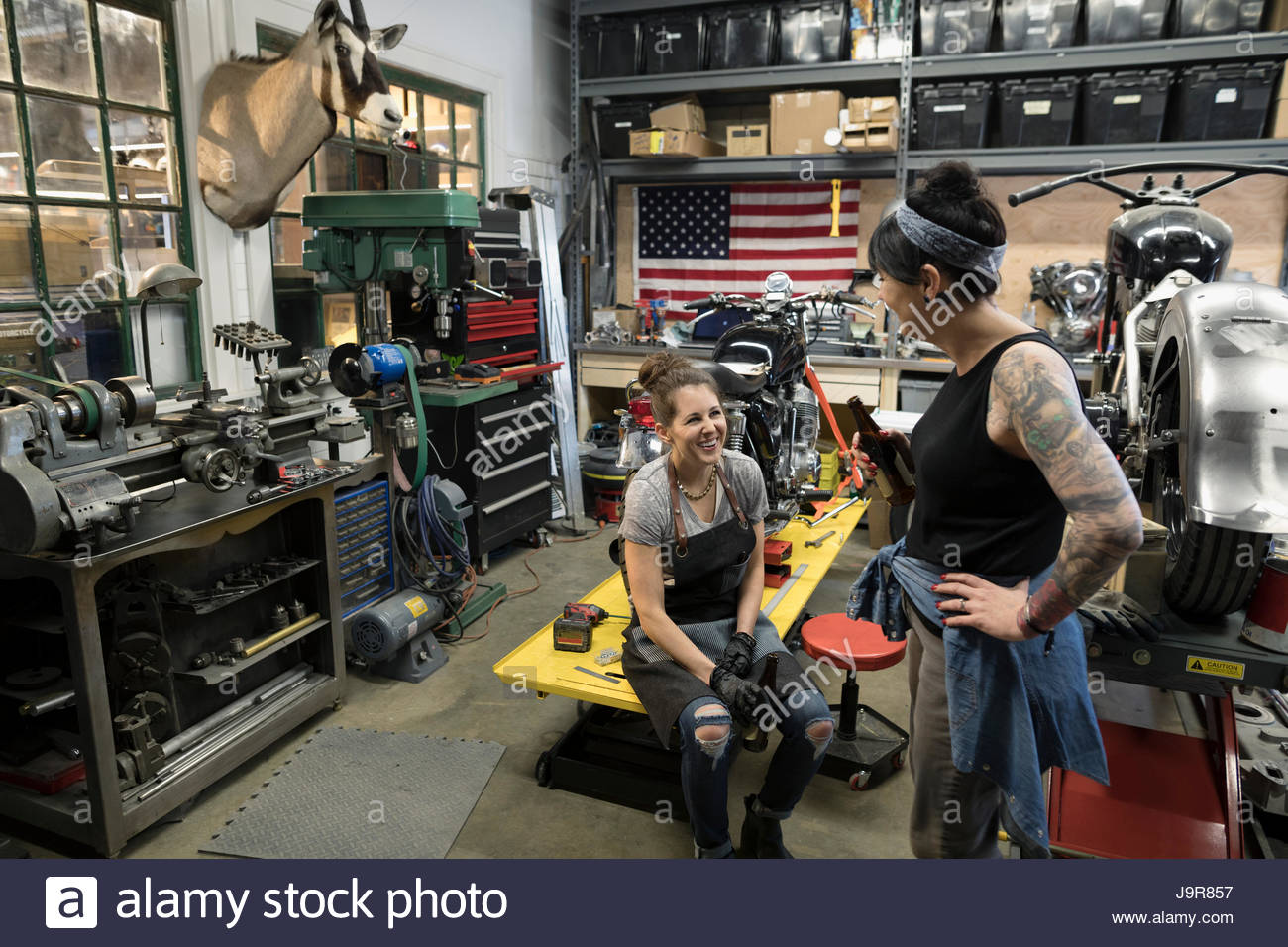 Female motorcycle mechanics talking, drinking beer in auto repair shop ...