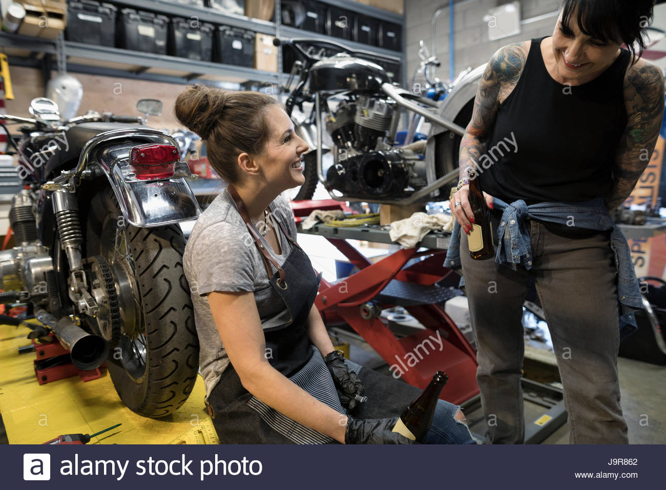 Female motorcycle mechanics talking, drinking beer in auto repair shop ...