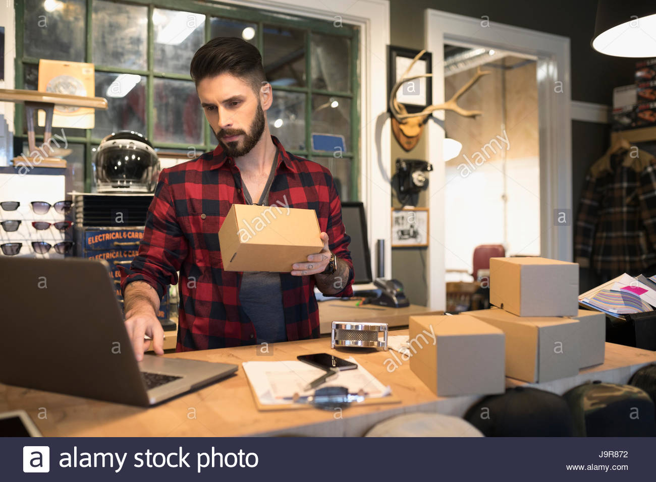 Motorcycle shop owner processing merchandise at laptop behind counter ...