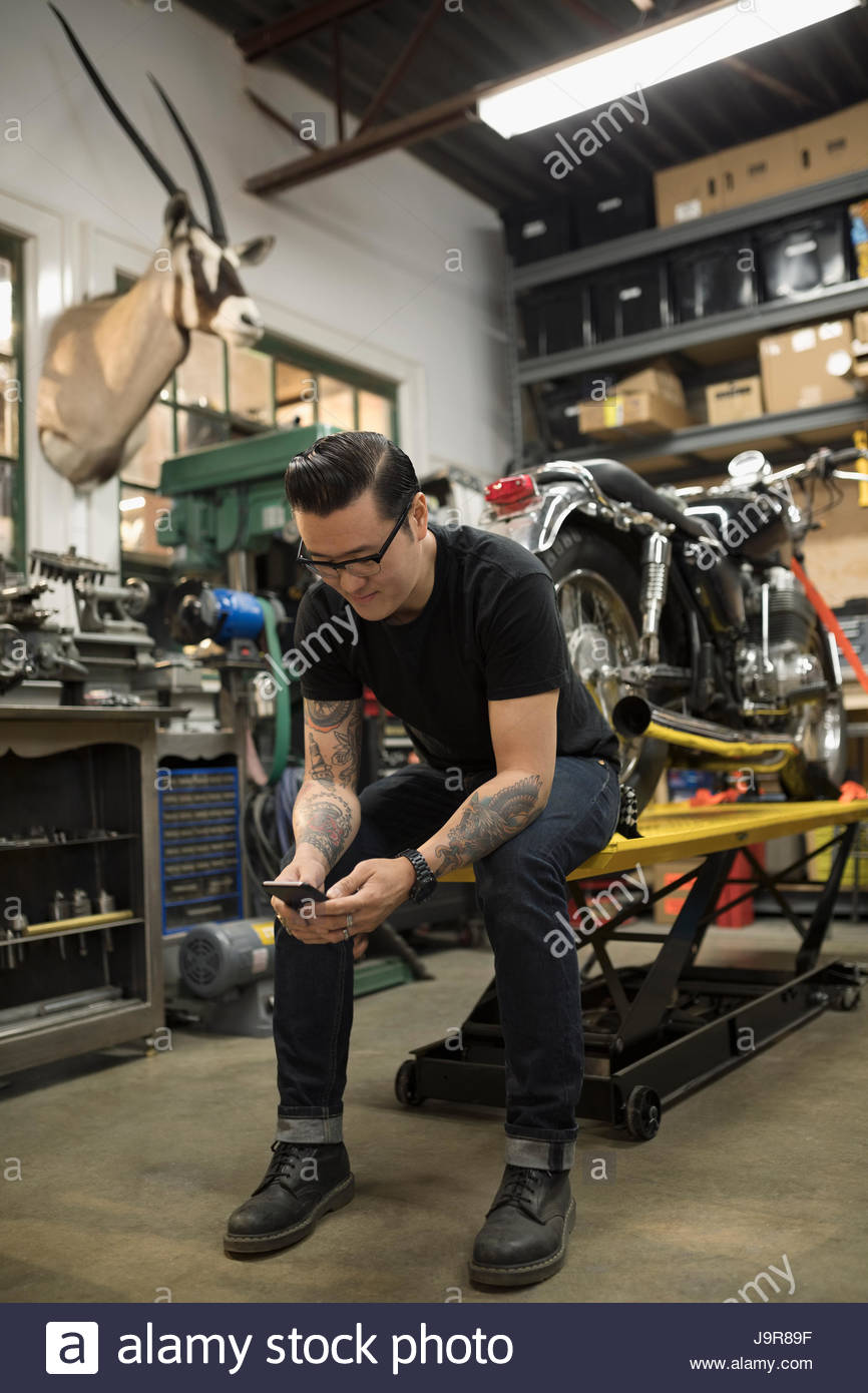 Motorcycle mechanic texting with cell phone in auto repair shop Stock ...