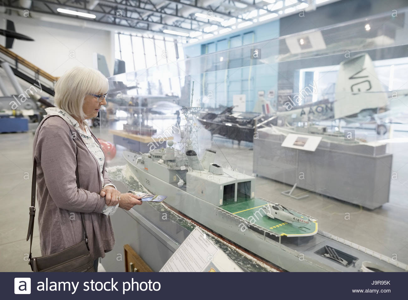 Senior woman looking at model Naval ship exhibit in war museum hangar ...