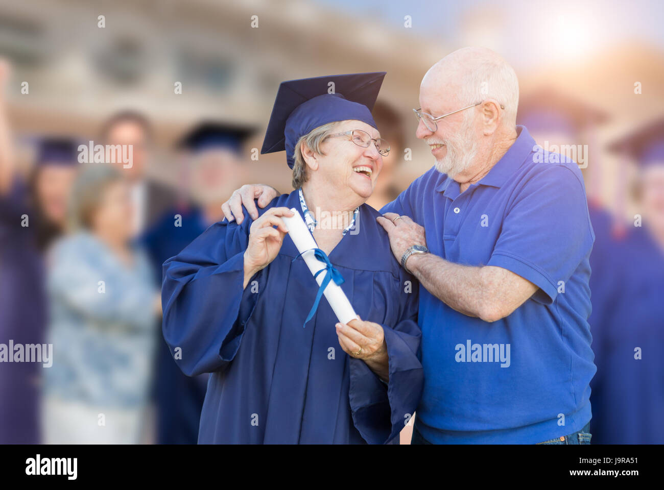 Senior Adult Woman In Cap and Gown Being Congratulated By Husband At ...
