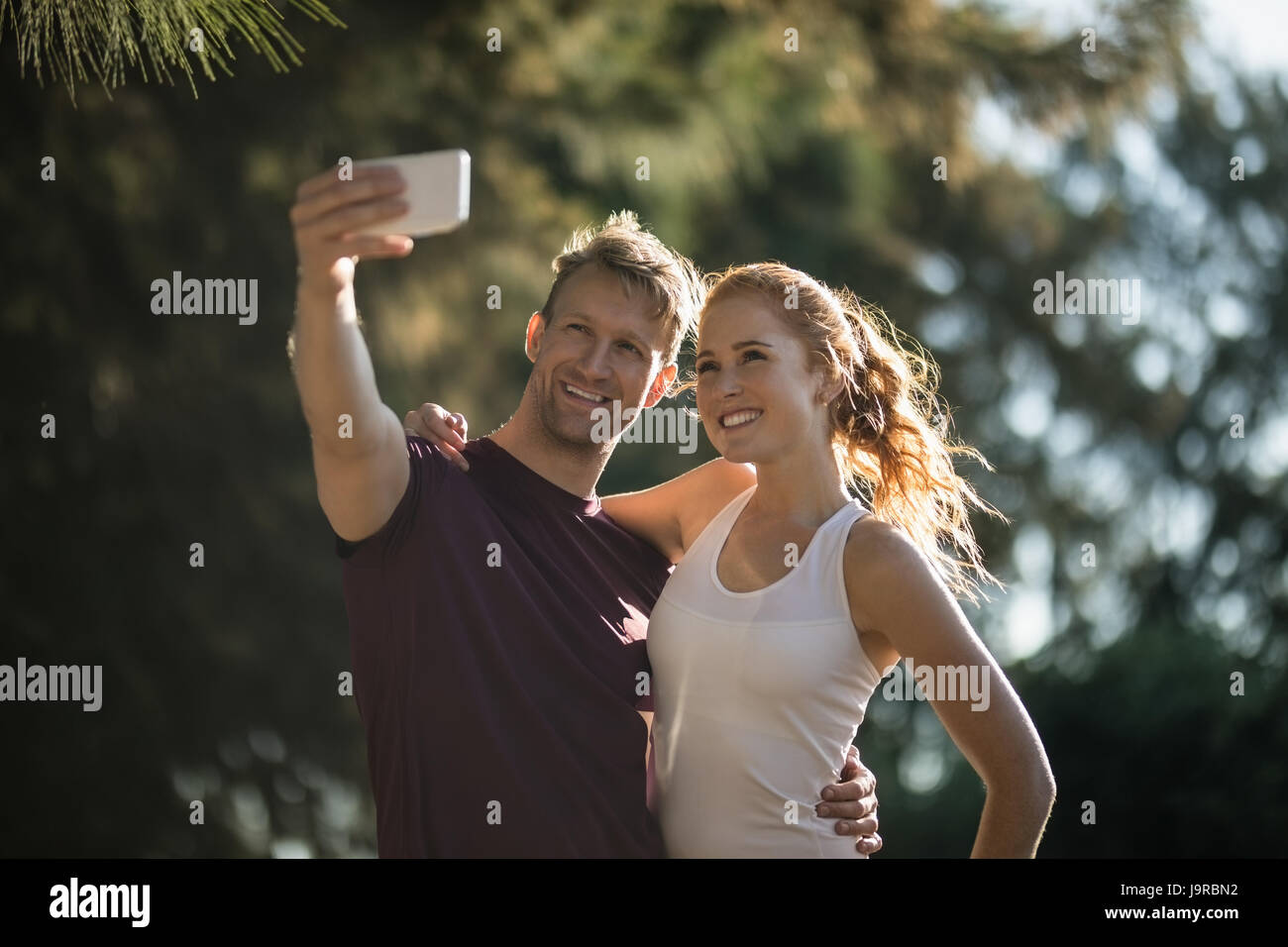 Low angle view of happy young couple taking selfie on sunny day at farm ...
