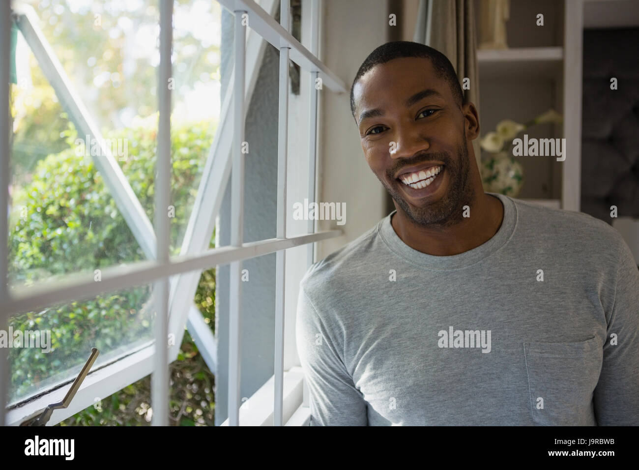 Portrait of smiling man standing by window at home Stock Photo - Alamy