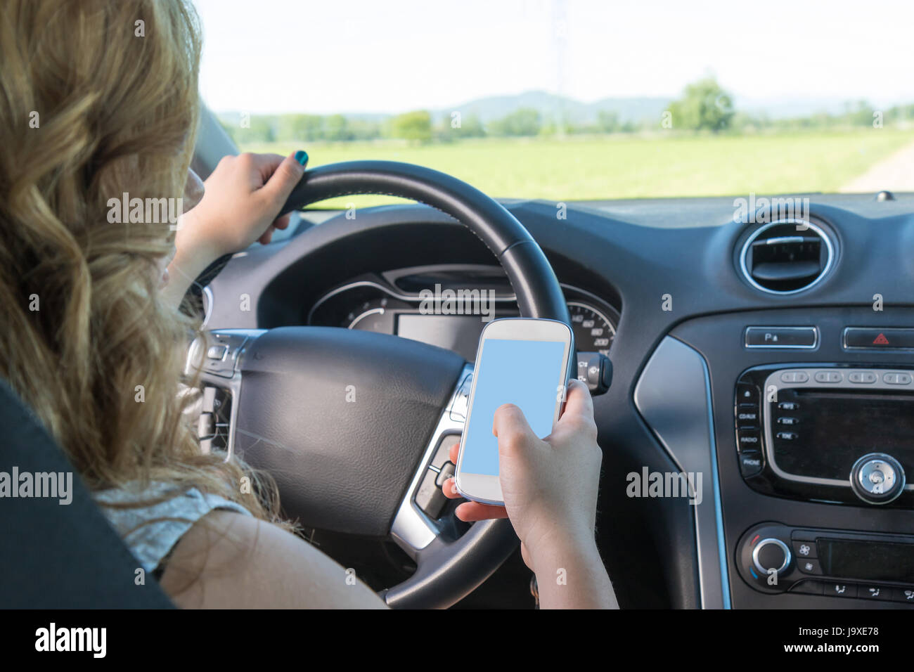 Young driver woman is using a smart phone while driving a car. View ...