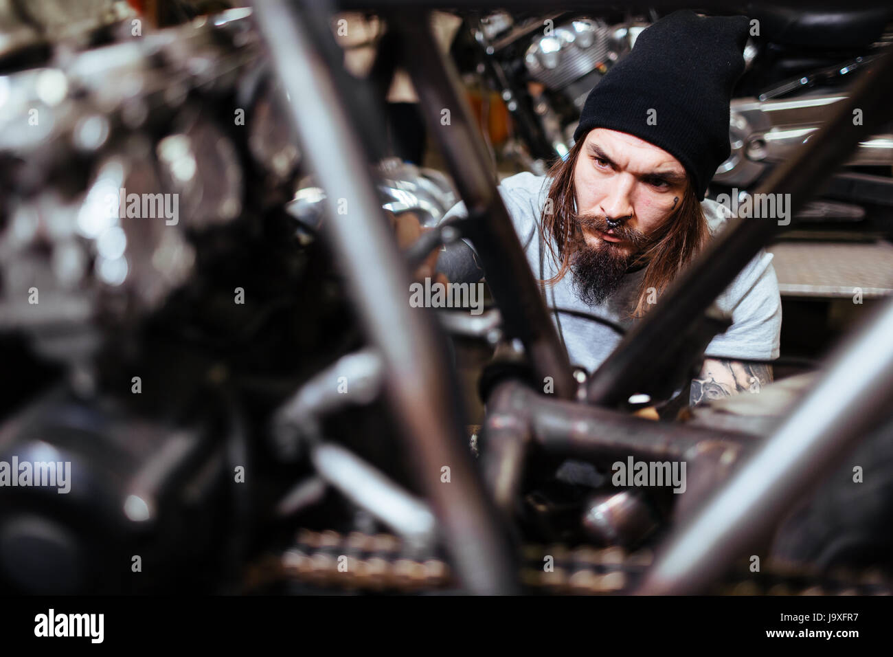 Portrait of focused tattooed man working in garage tuning up motorcycle ...