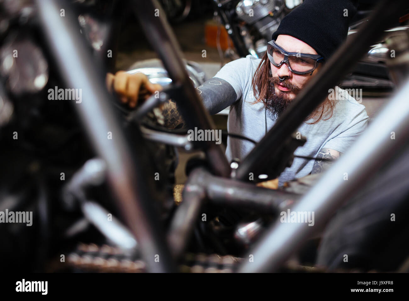 Portrait of tattooed man working in garage customizing motorcycle and ...