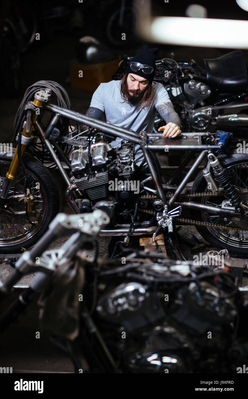 Portrait of modern heavily tattooed man assembling custom motorcycle in ...