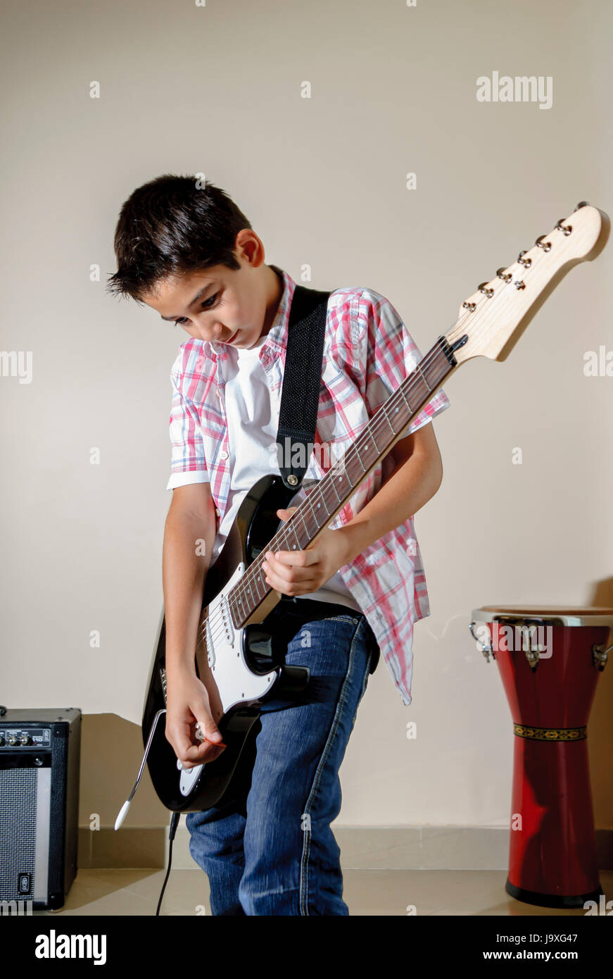Teen boy playing electric guitar at home isolated over yellow warm ...