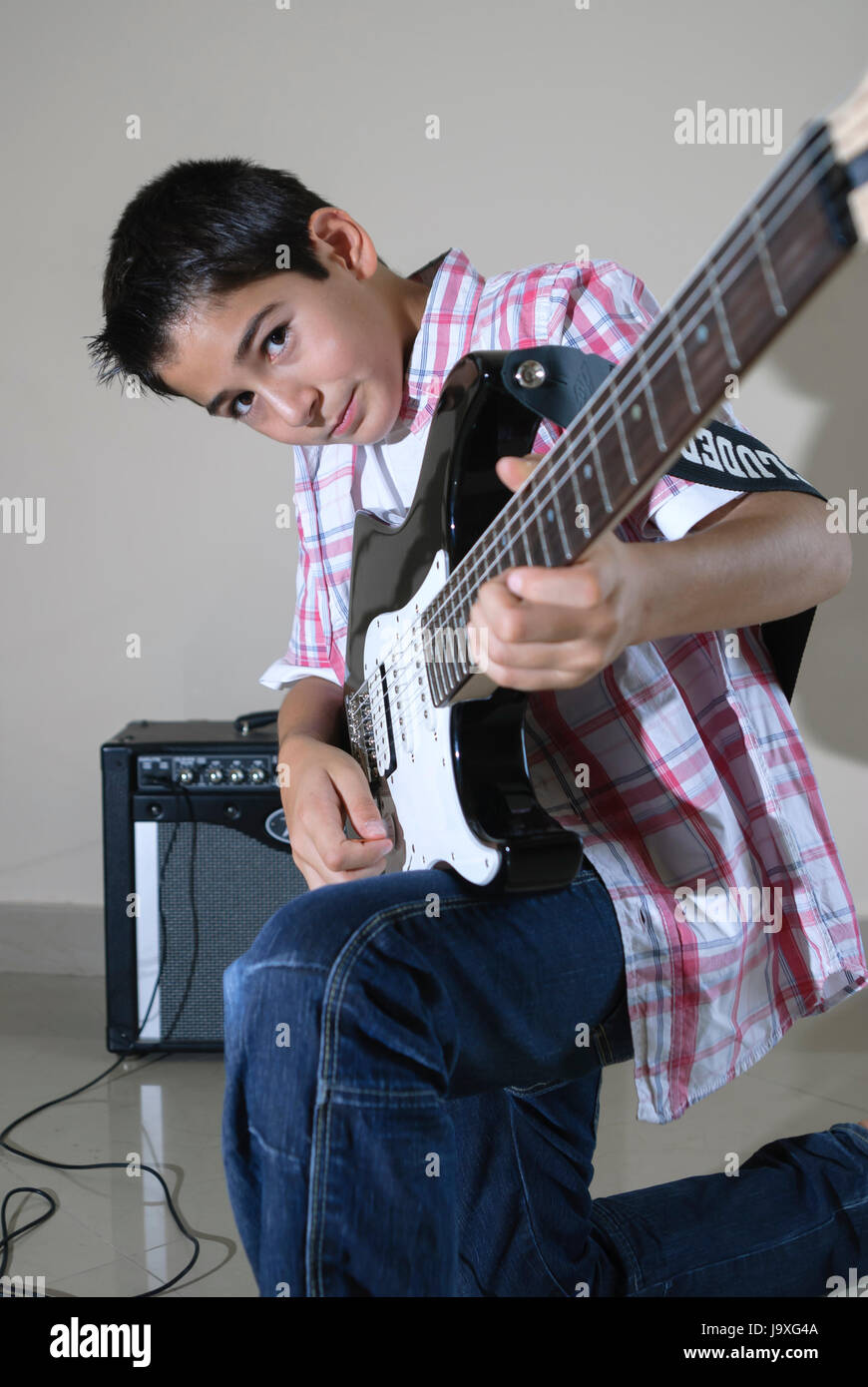 Teen boy playing electric guitar isolated over withe gray background ...