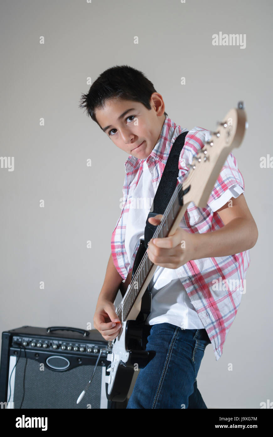 Teen boy playing electric guitar isolated over withe gray background ...