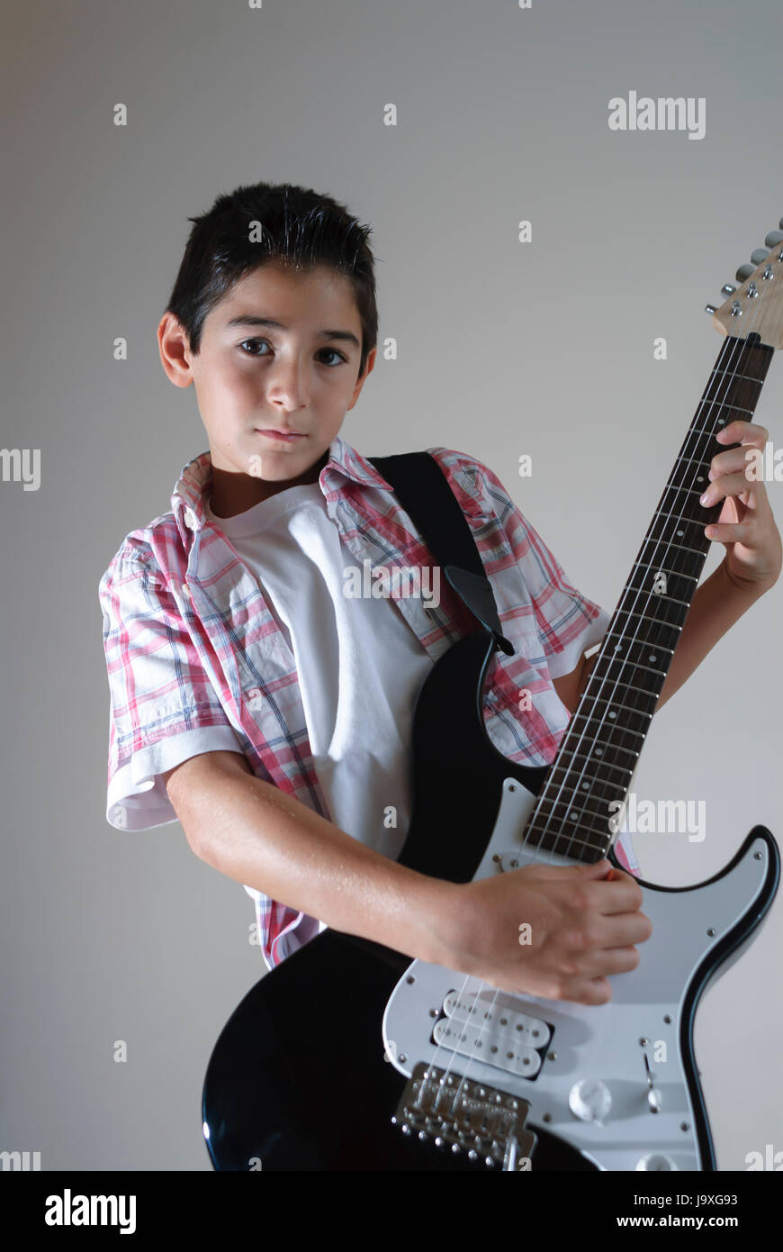Teen boy playing electric guitar isolated over withe gray background ...