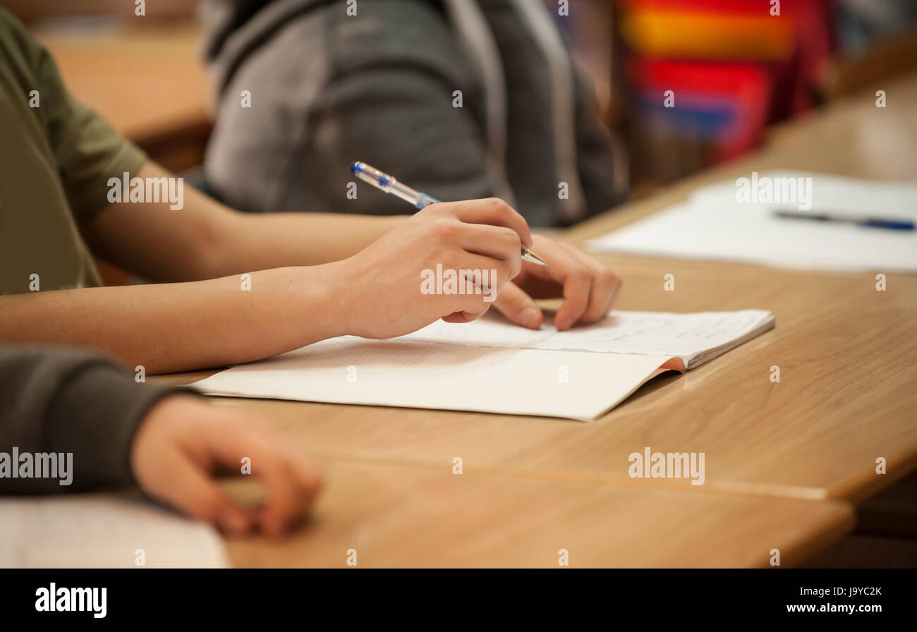 Closeup of student hands on the school table in the classroom writing ...